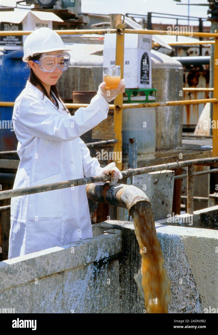 Chemist taking a sample from a stream of industrial waste slurry to ...