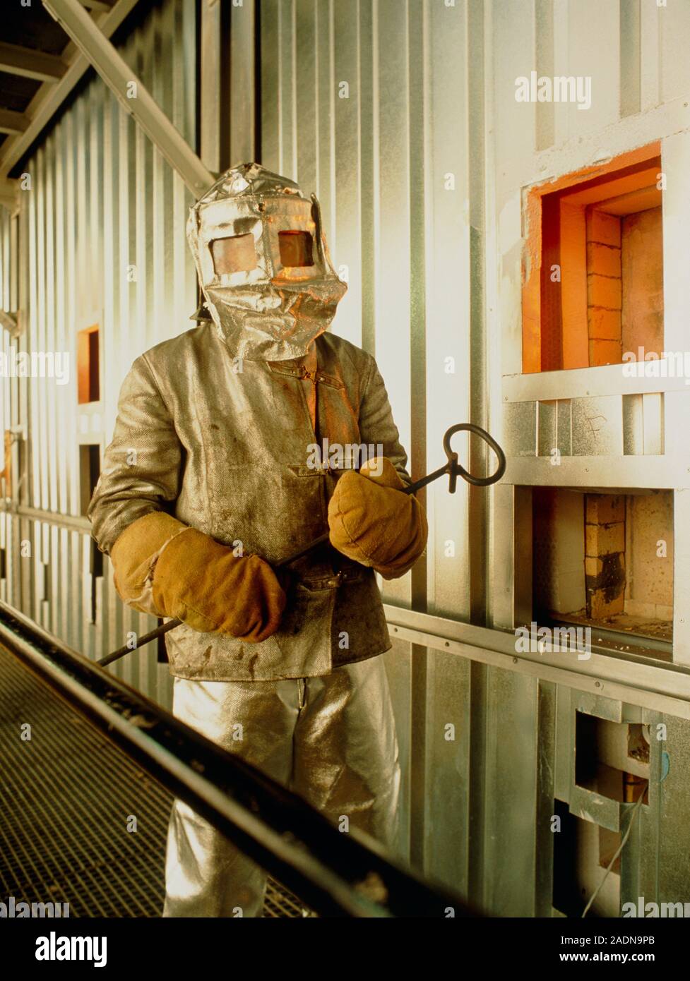 Glass production. Technician in safety clothing beside a furnace for ...