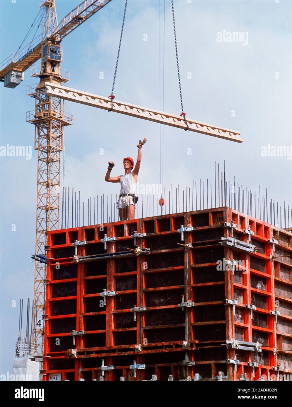 Building site. Construction worker receiving a crane load on top of a ...