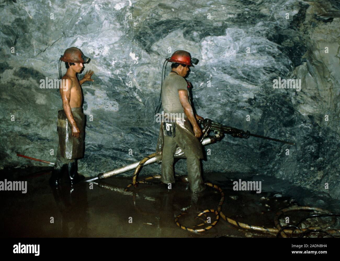 Standing ankle deep in water, miners drill rock to place explosives ...