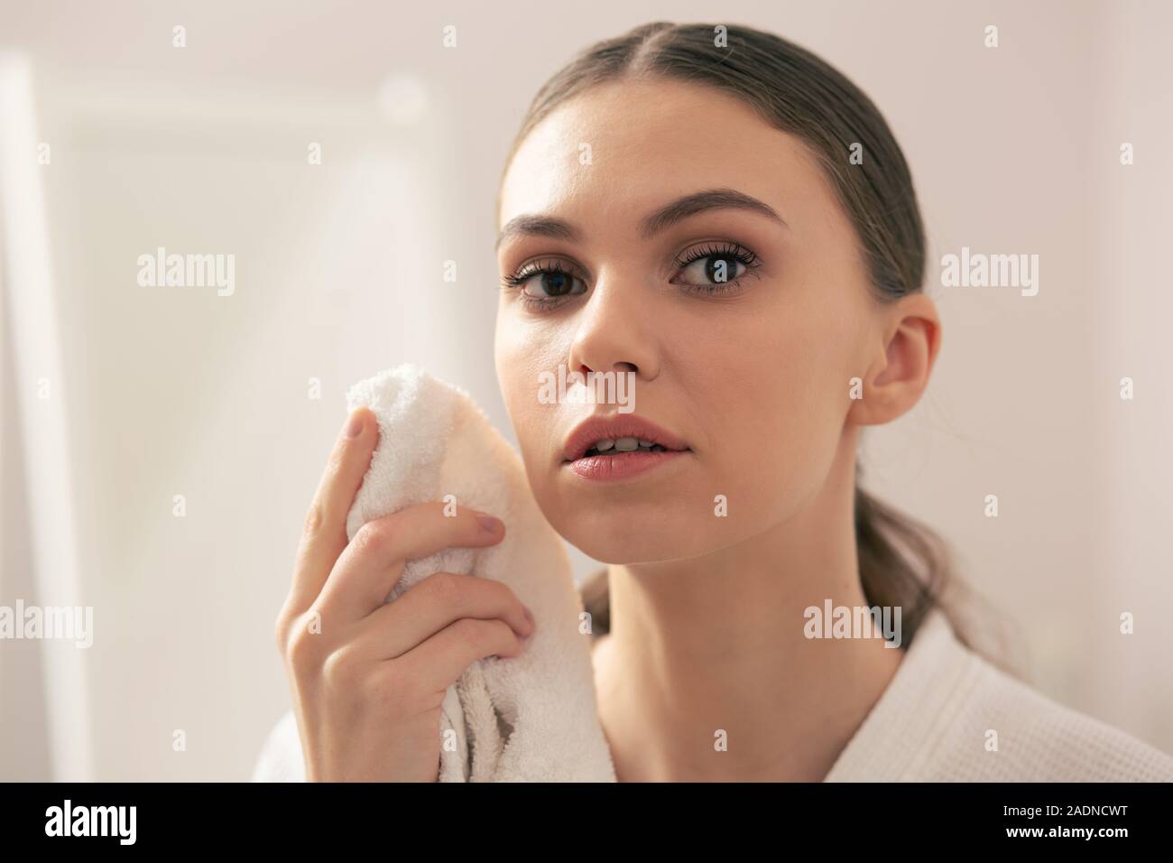 Thoughtful young woman touching her face with soft towel Stock Photo ...
