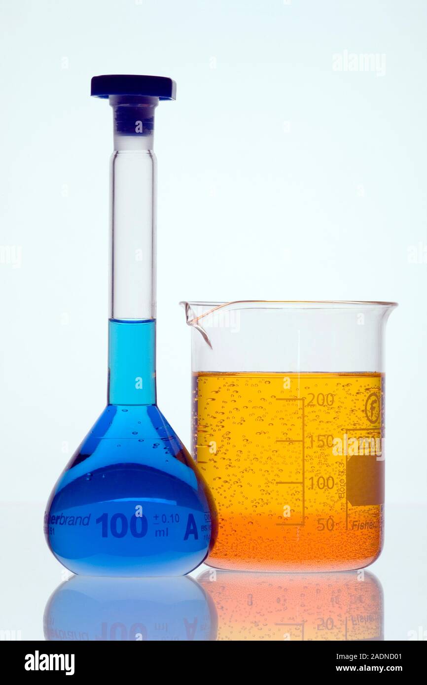 Laboratory glassware. Volumetric flask and beaker containing coloured ...