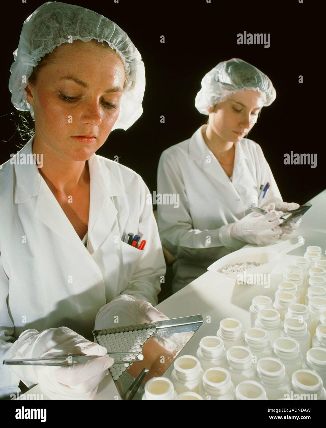 Counting pills. Female technicians in protective clothing using tablet ...