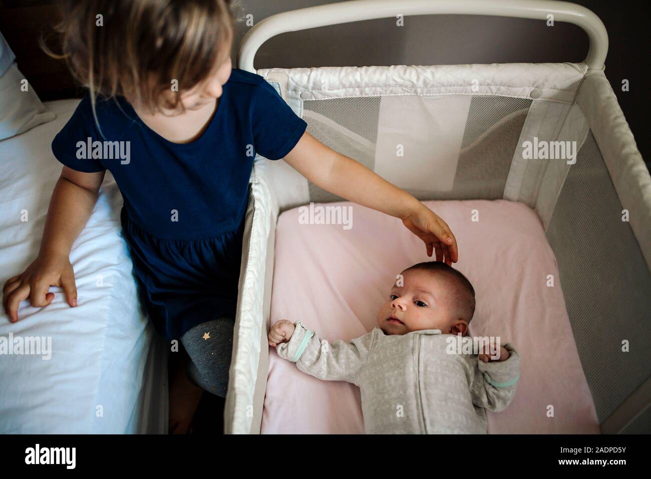 4 yr old touching head of newborn sister in crib with pink sheet Stock ...