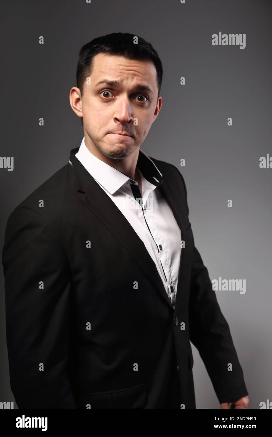 Surprising grimacing man looking in black suit with funny face on grey ...