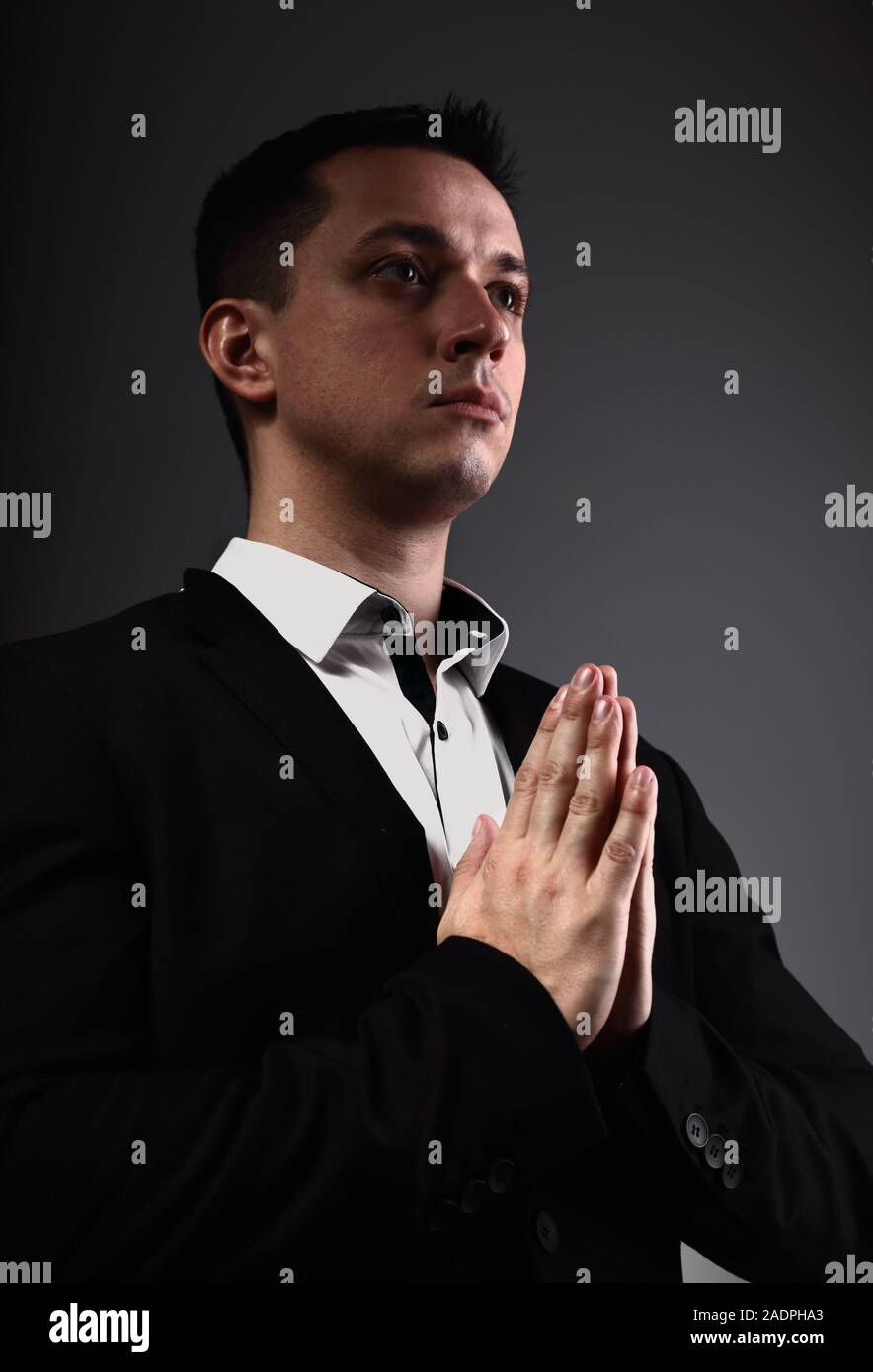 Serious thinking man praying and gestering the hands in black suit on ...