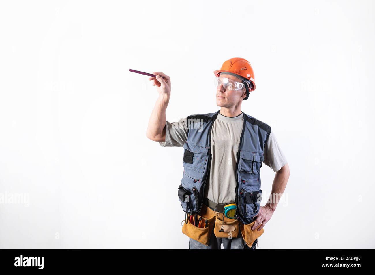 A builder in a helmet makes visual measurement with a marking pencil ...