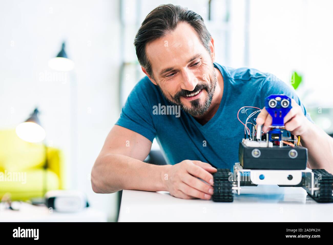 Waist up of a smiling bearded man testing his modern robot Stock Photo ...