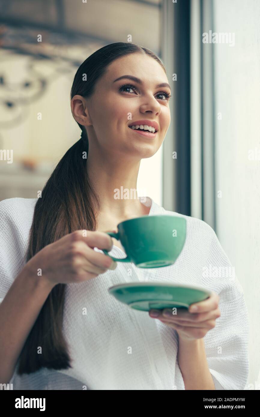 Positive long haired lady smiling and holding her cup Stock Photo - Alamy