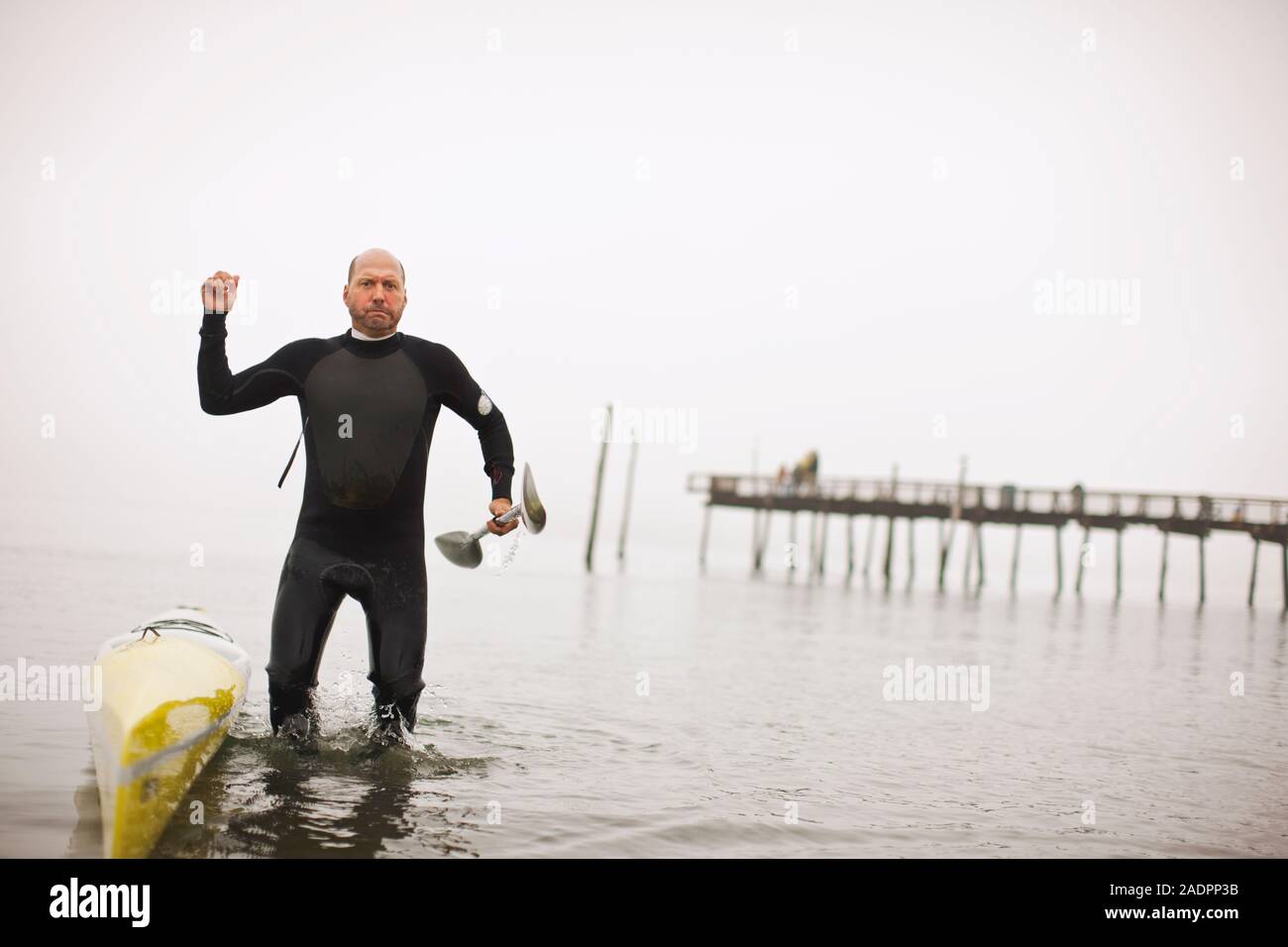 Male kayaker makes a silly face and jumps as he poses with a kayak and ...