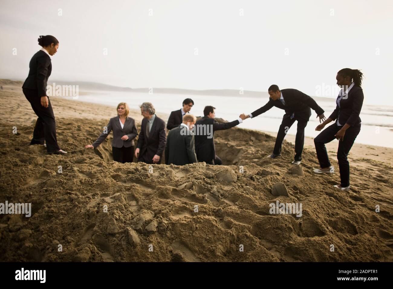 Businesspeople climbing out of hole in sand on the beach Stock Photo ...