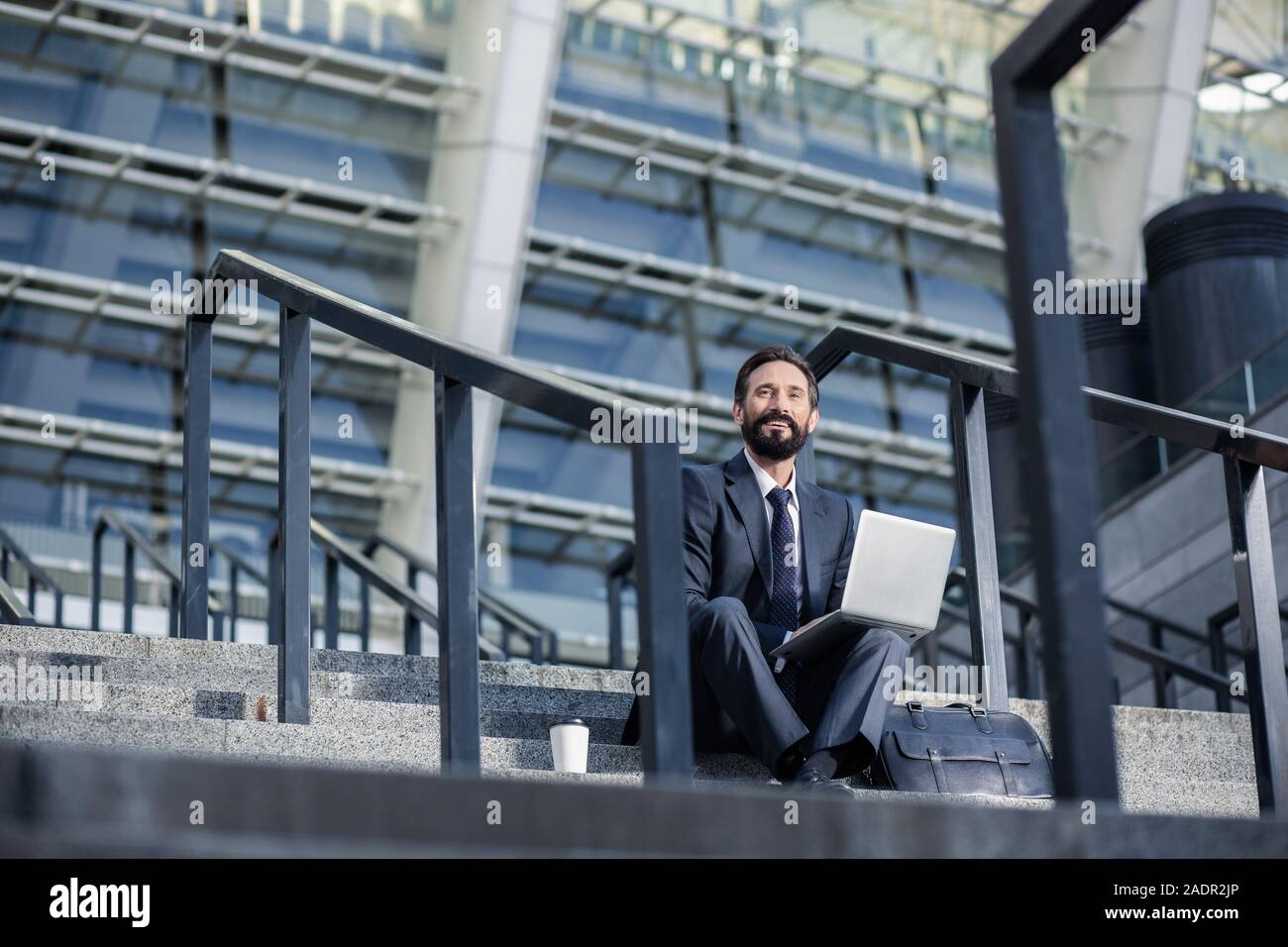 Low angle of a smiling businessman using laptop on the staircases Stock ...