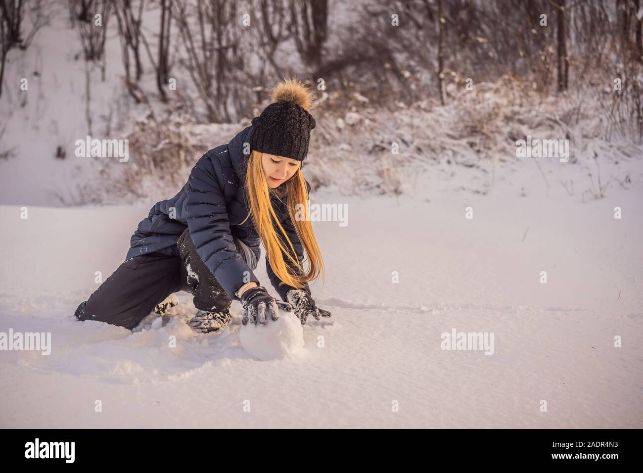 Young woman rolling giant snowball to make snowman Stock Photo - Alamy