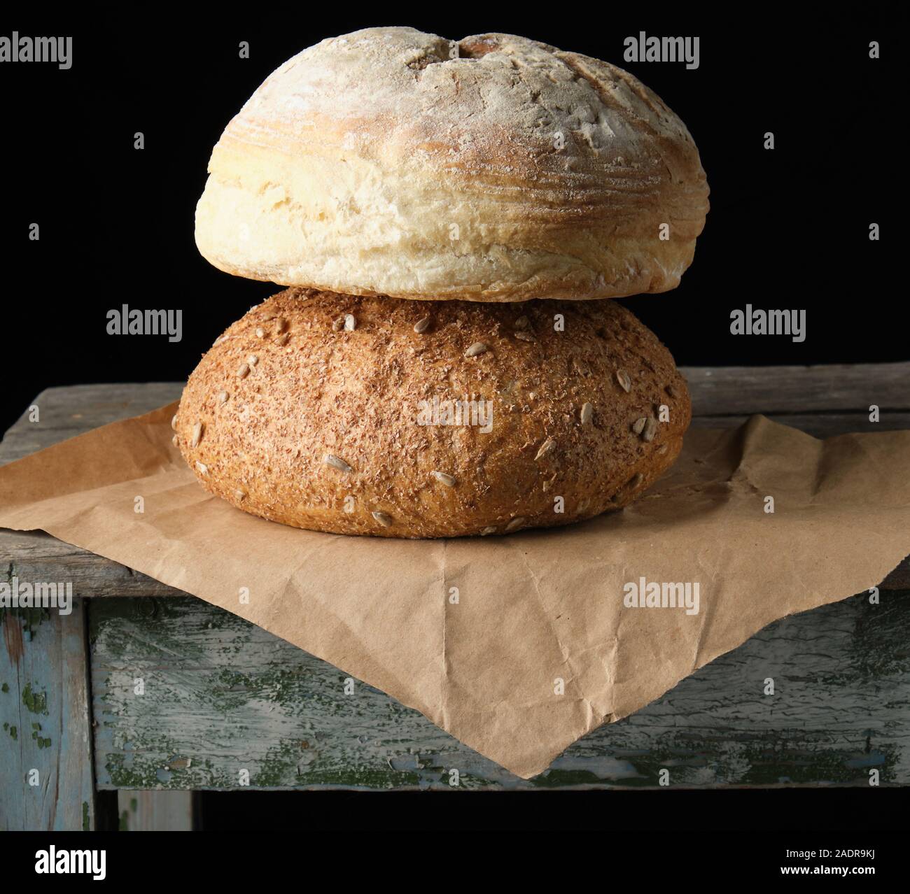 two loaves of baked round bread lay on brown paper, black background ...