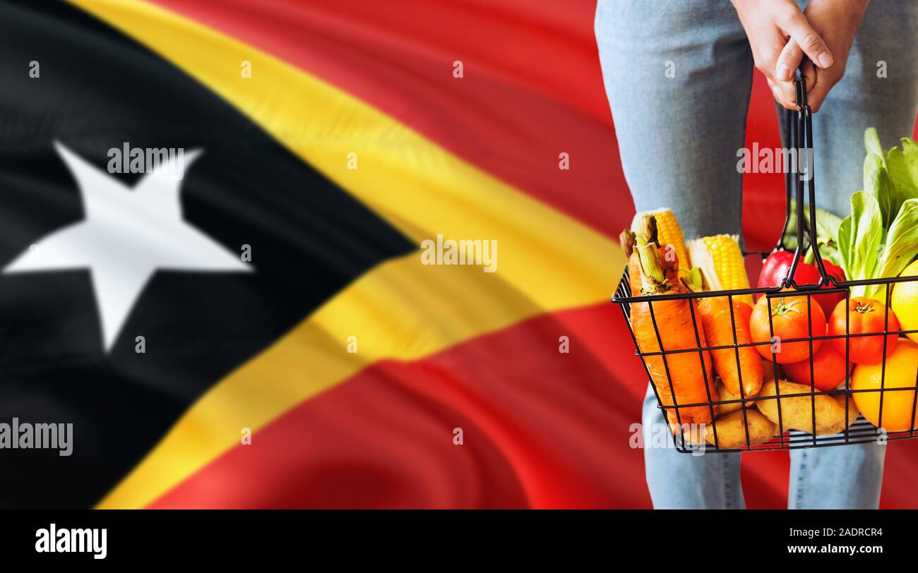 Woman is holding supermarket basket, East Timor waving flag background ...