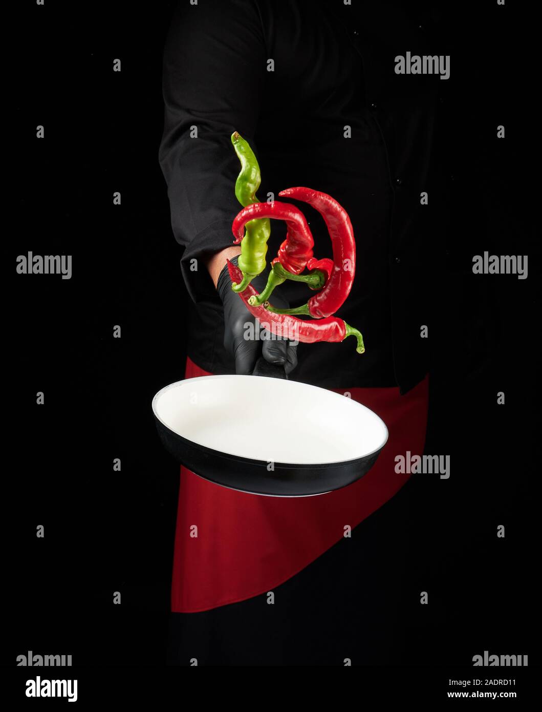 chef in black uniform and red apron holds a round pan with fresh chili ...