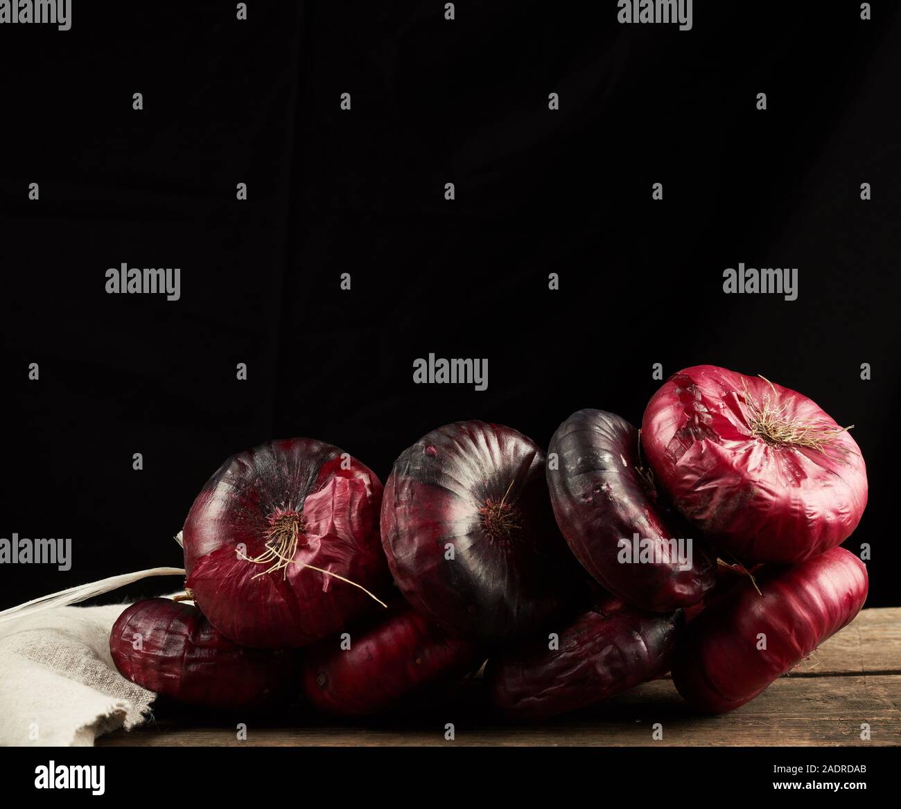 round red onion in husk on a gray linen napkin, black background, close ...