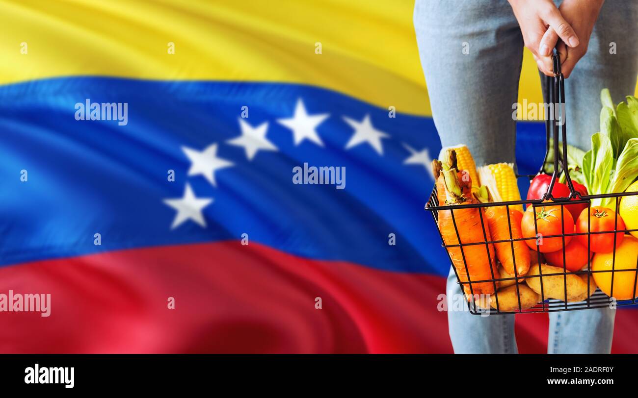 Woman is holding supermarket basket, Venezuela waving flag background ...