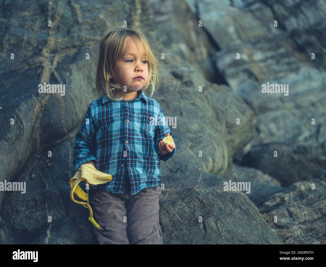 A little toddler is eating a banana by some rocks Stock Photo - Alamy