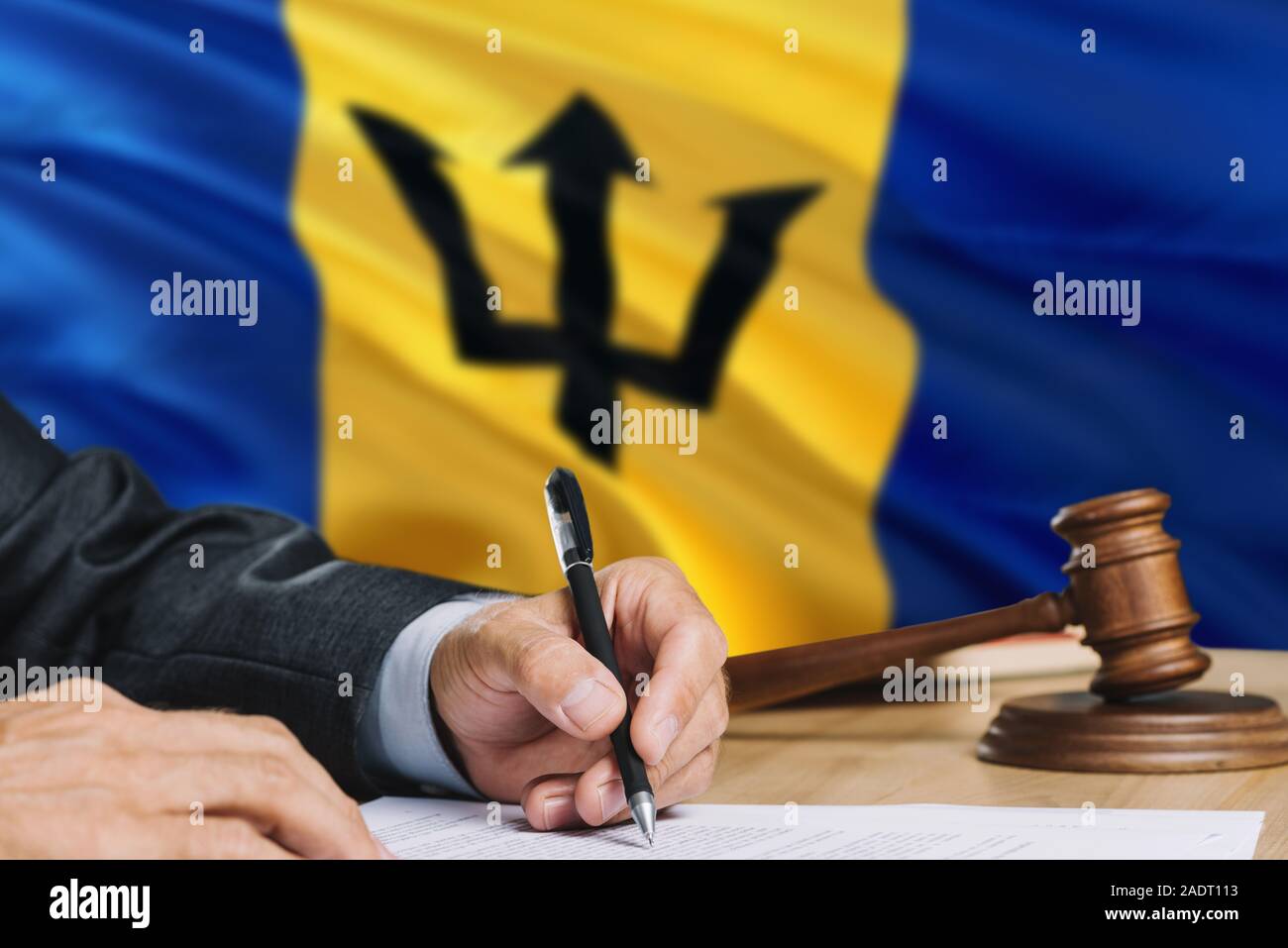Judge writing on paper in courtroom with Barbados flag background ...