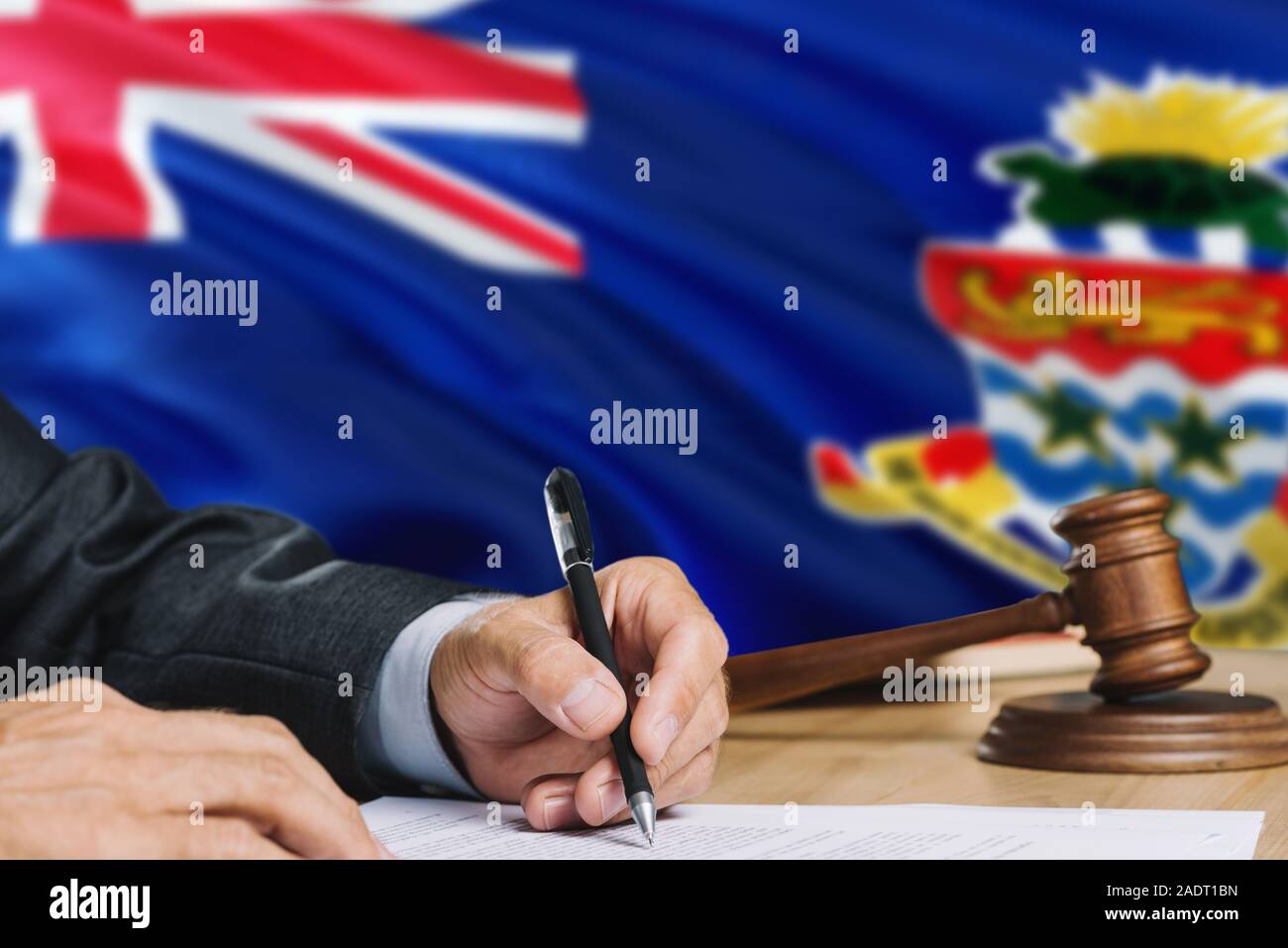 Judge writing on paper in courtroom with Cayman Islands flag background ...