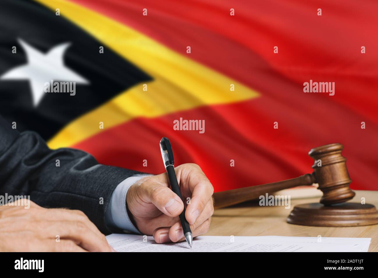 Judge writing on paper in courtroom with East Timor flag background ...