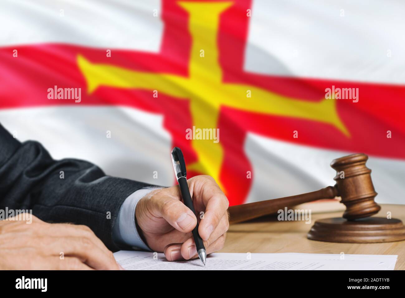 Judge writing on paper in courtroom with Guernsey flag background ...