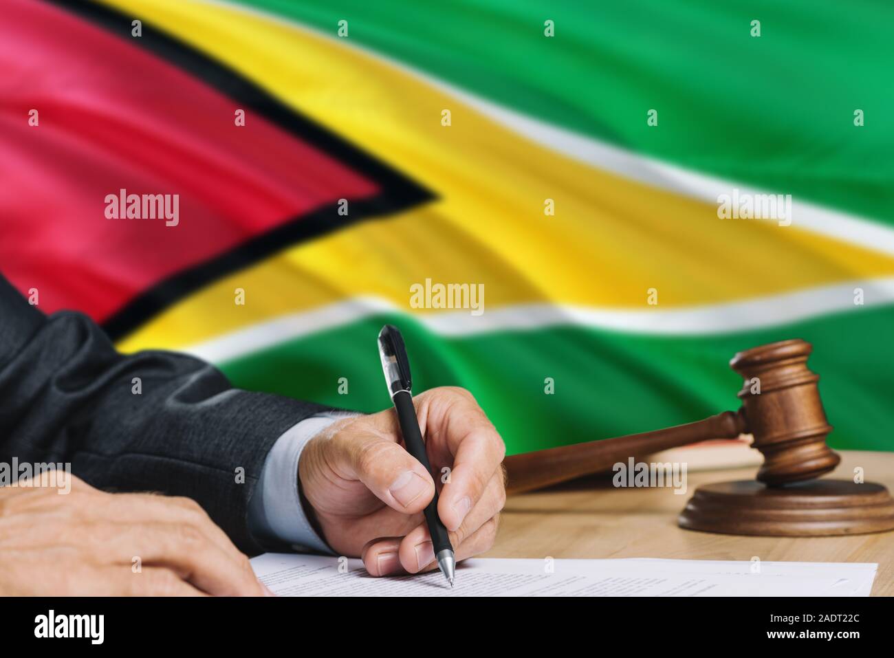 Judge writing on paper in courtroom with Guyana flag background. Wooden ...