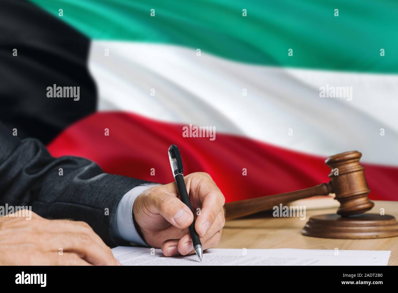 Judge writing on paper in courtroom with Kuwait flag background. Wooden ...
