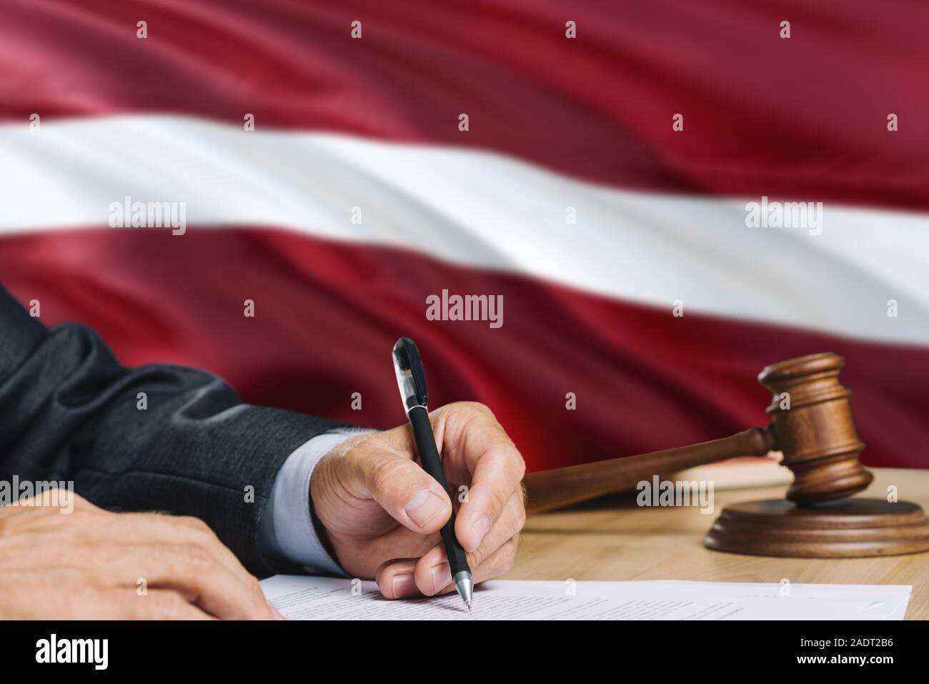 Judge writing on paper in courtroom with Latvia flag background. Wooden ...