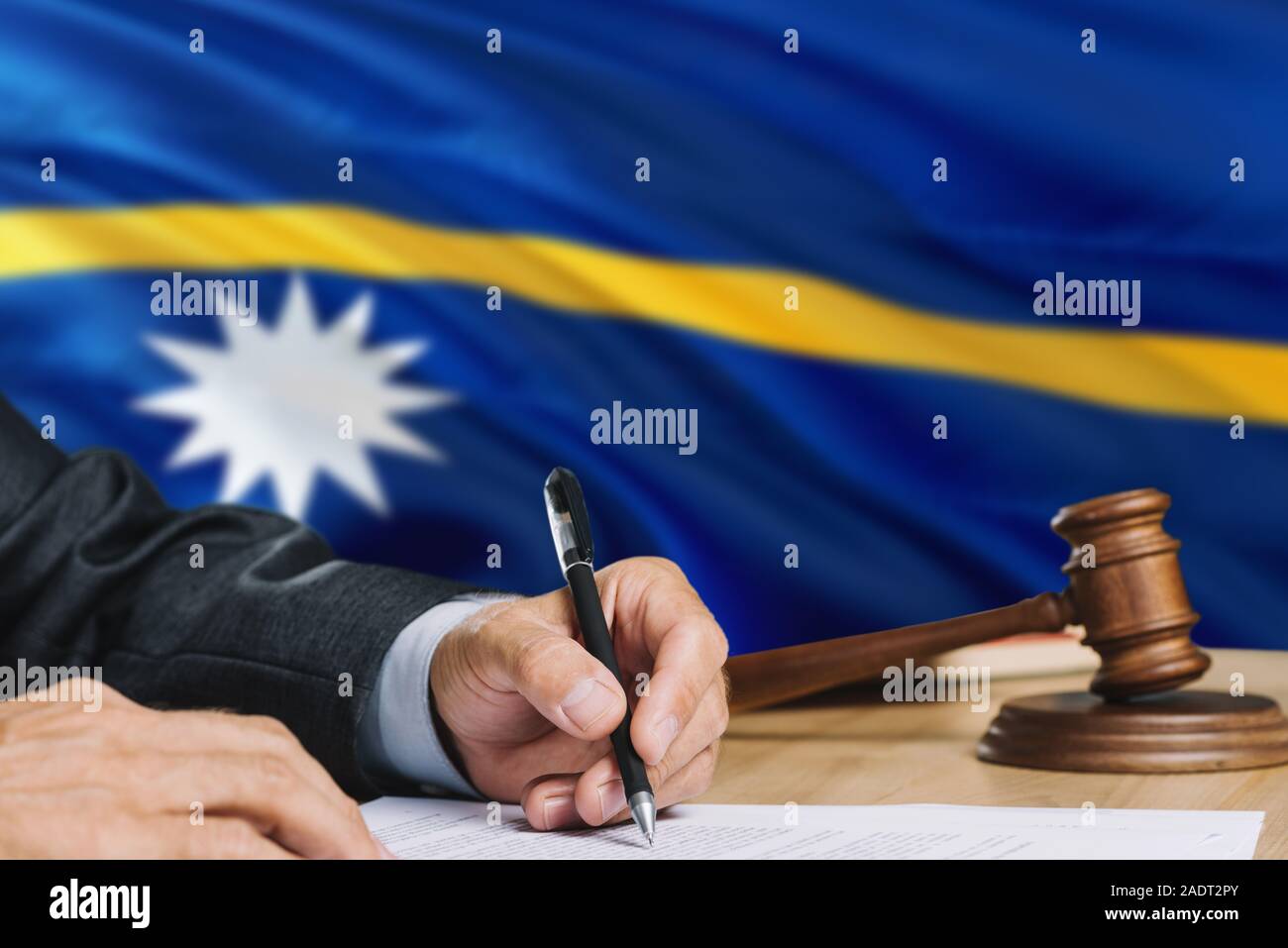 Judge writing on paper in courtroom with Nauru flag background. Wooden ...