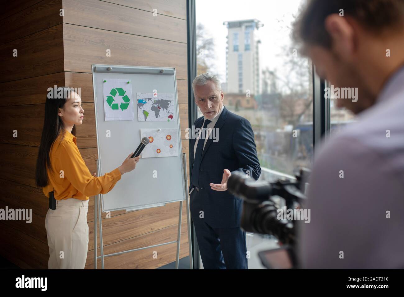 Dark-haired female reporter standing near the white board Stock Photo ...