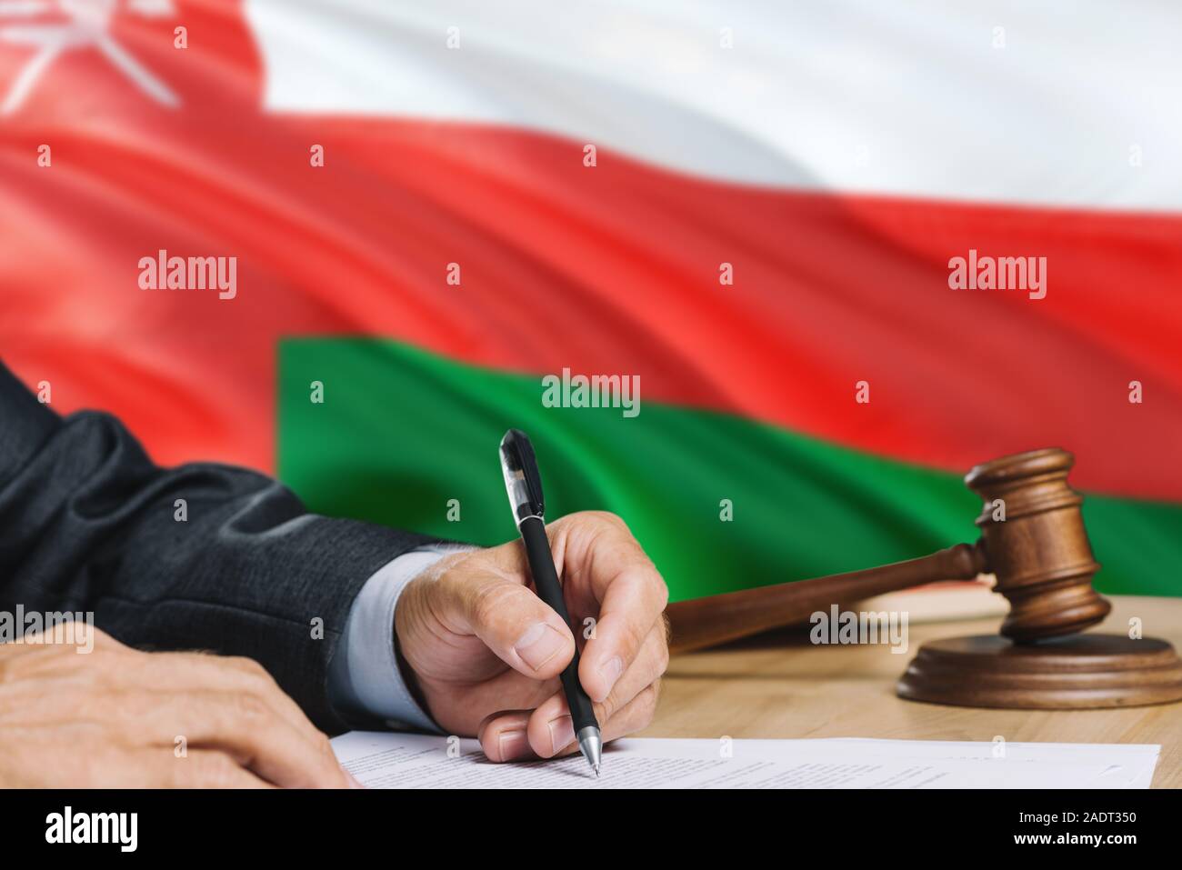Judge writing on paper in courtroom with Oman flag background. Wooden ...
