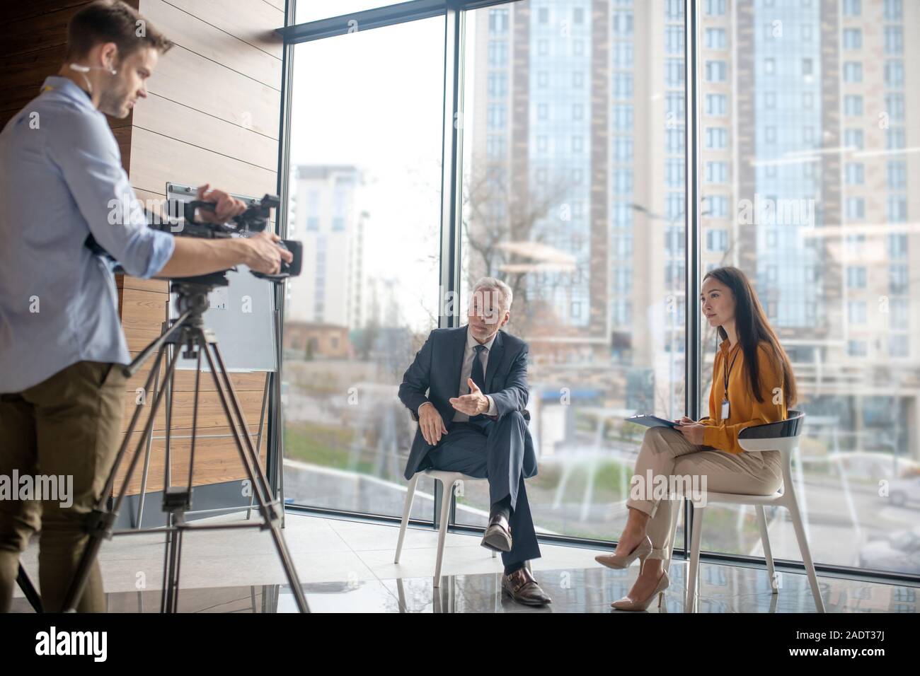 Asian female reporter siting in the studio talking to a greay-haired ...