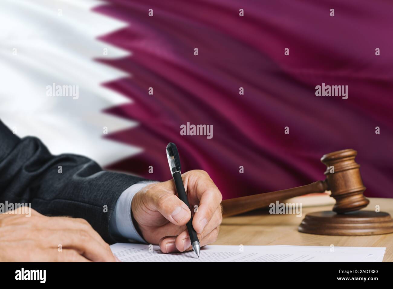 Judge writing on paper in courtroom with Qatar flag background. Wooden ...
