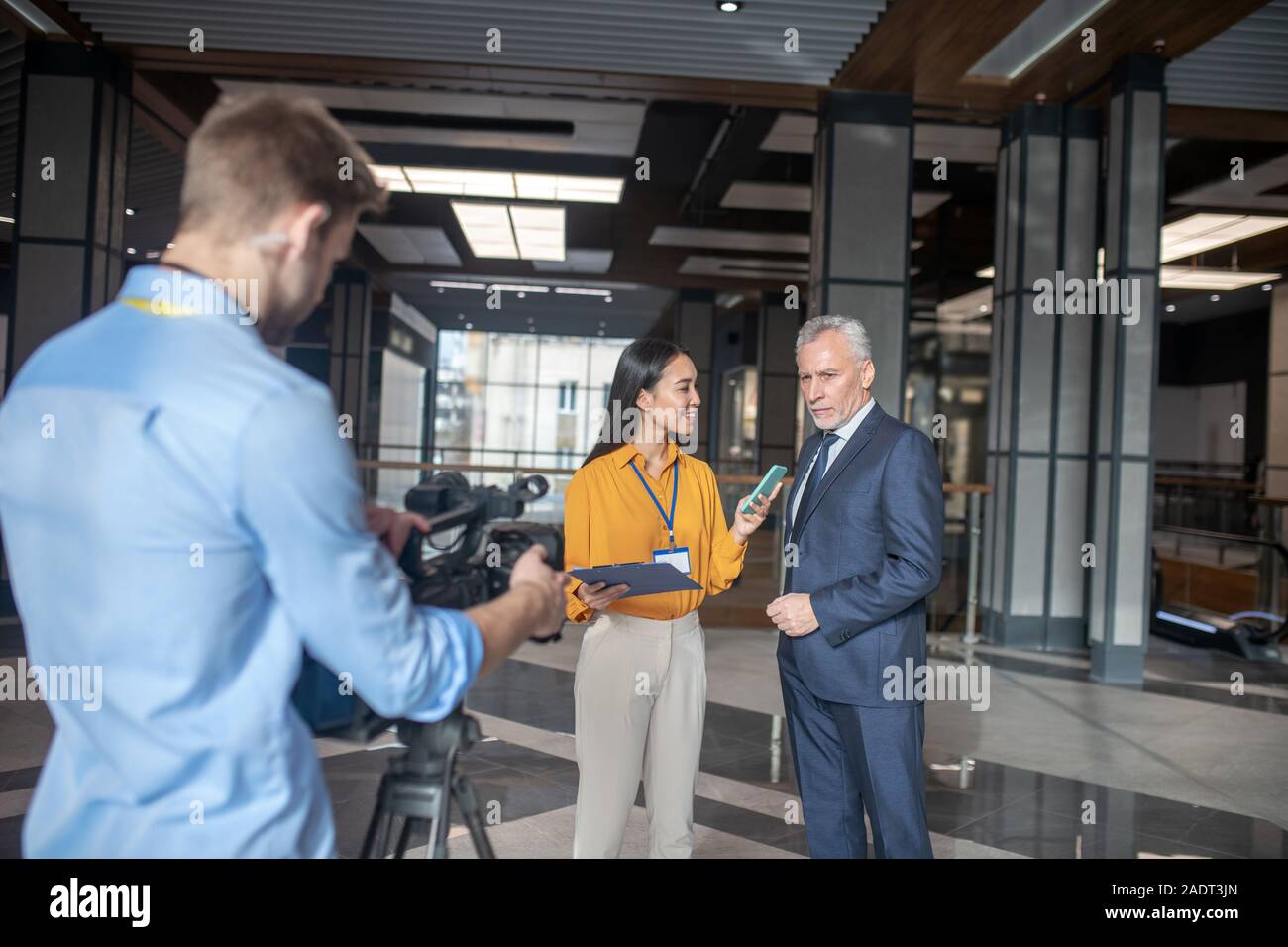 Asian female reporter standing next to grey-haired man Stock Photo - Alamy