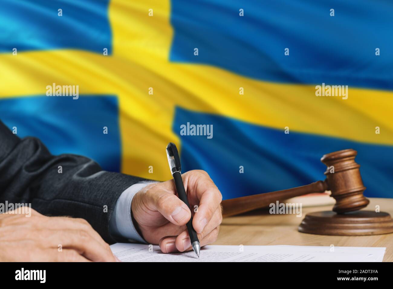 Judge writing on paper in courtroom with Sweden flag background. Wooden ...