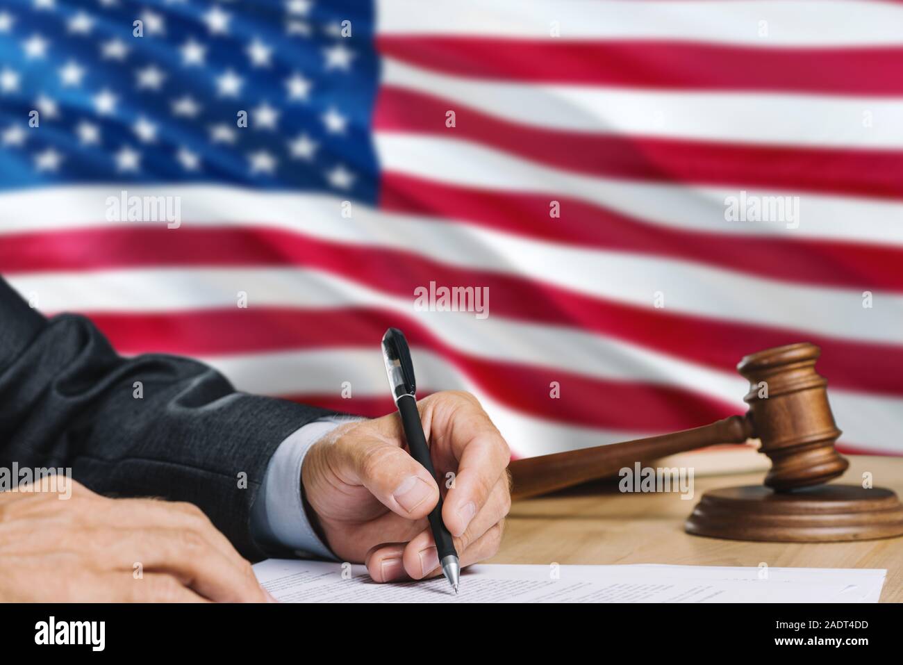 Judge writing on paper in courtroom with United States flag background ...