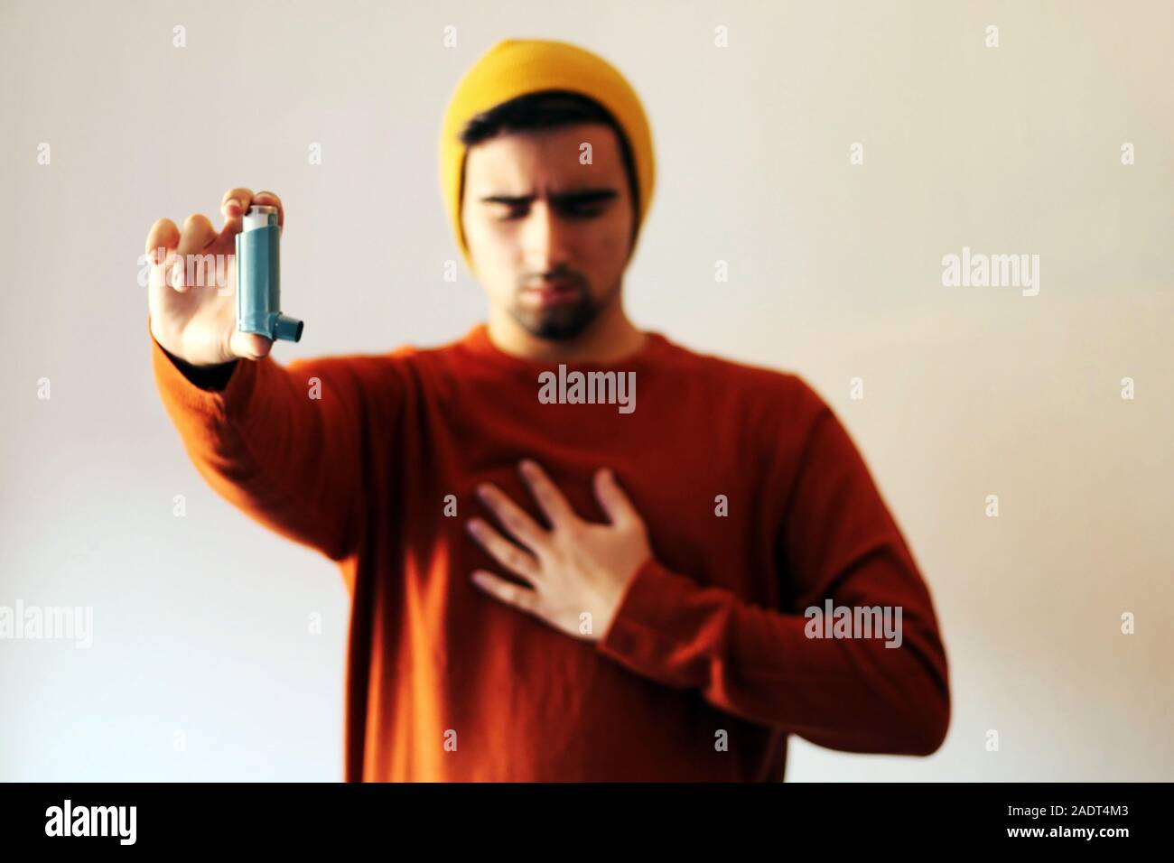 Man dressed in orange and wearing a yellow cap using a blue asthma ...