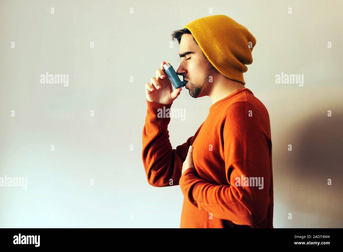 Man dressed in orange and wearing a yellow cap using a blue asthma ...