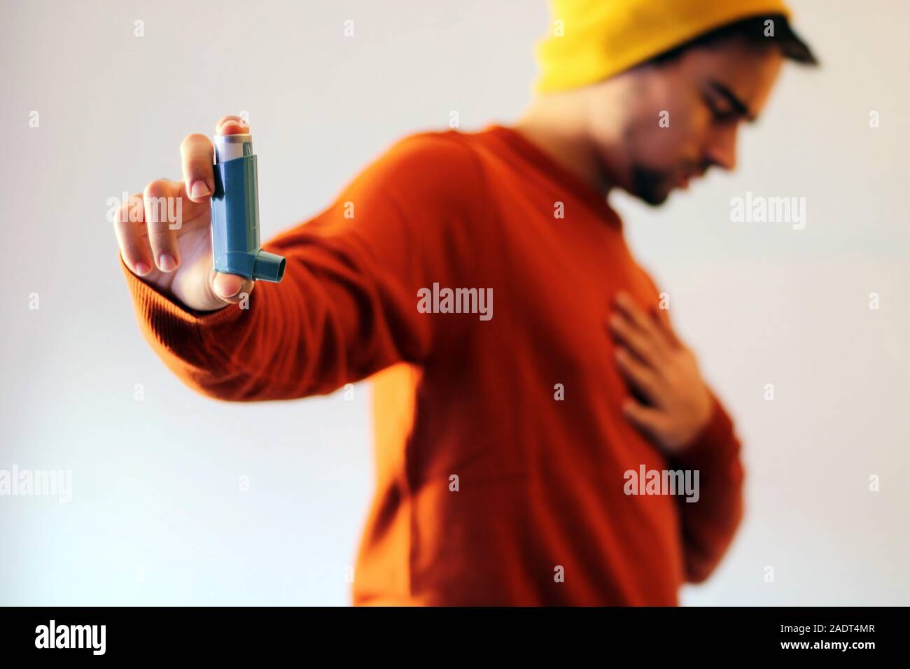 Man dressed in orange and wearing a yellow cap using a blue asthma ...
