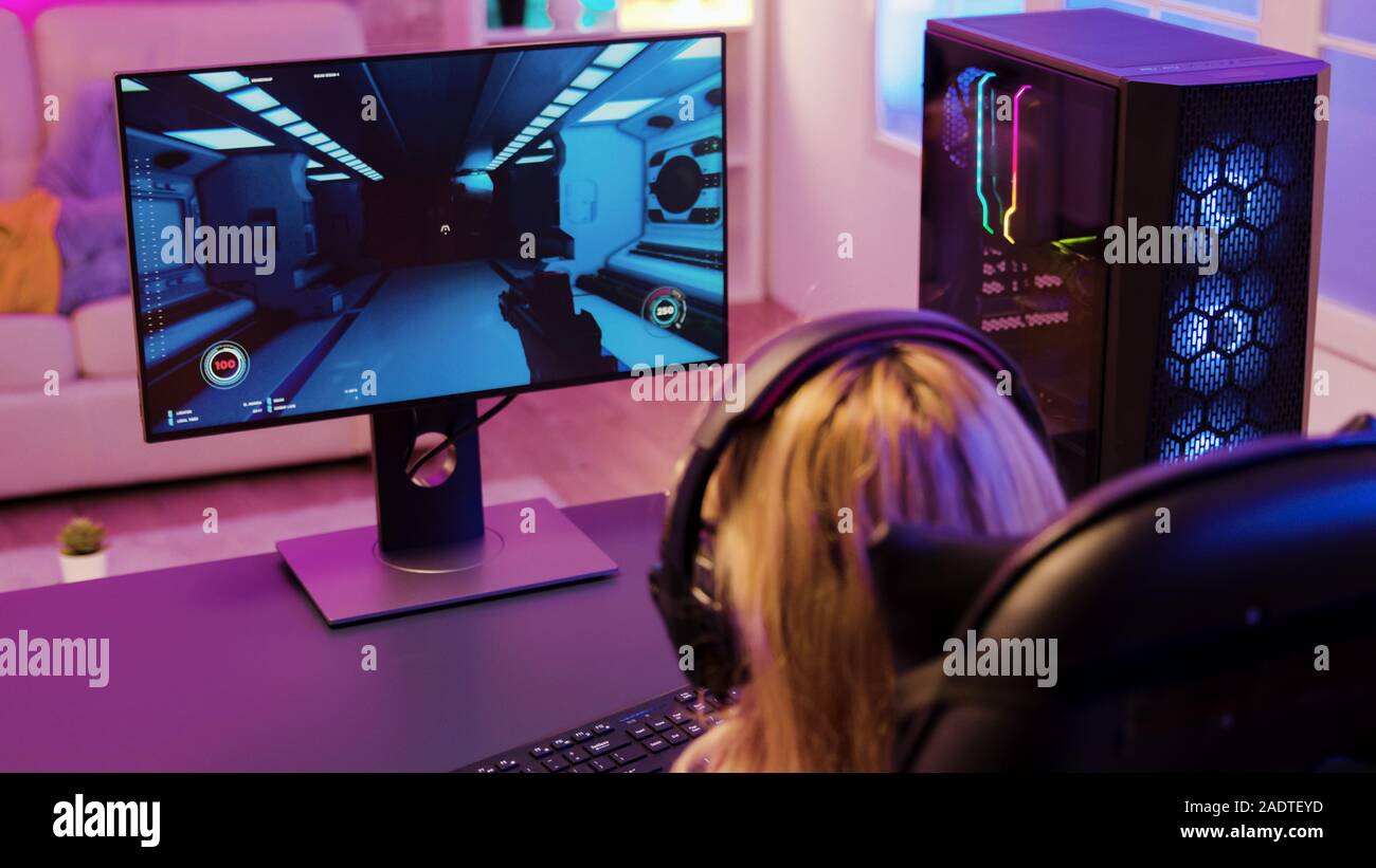 Back view of cheerful young girl playing shooter games sitting on ...