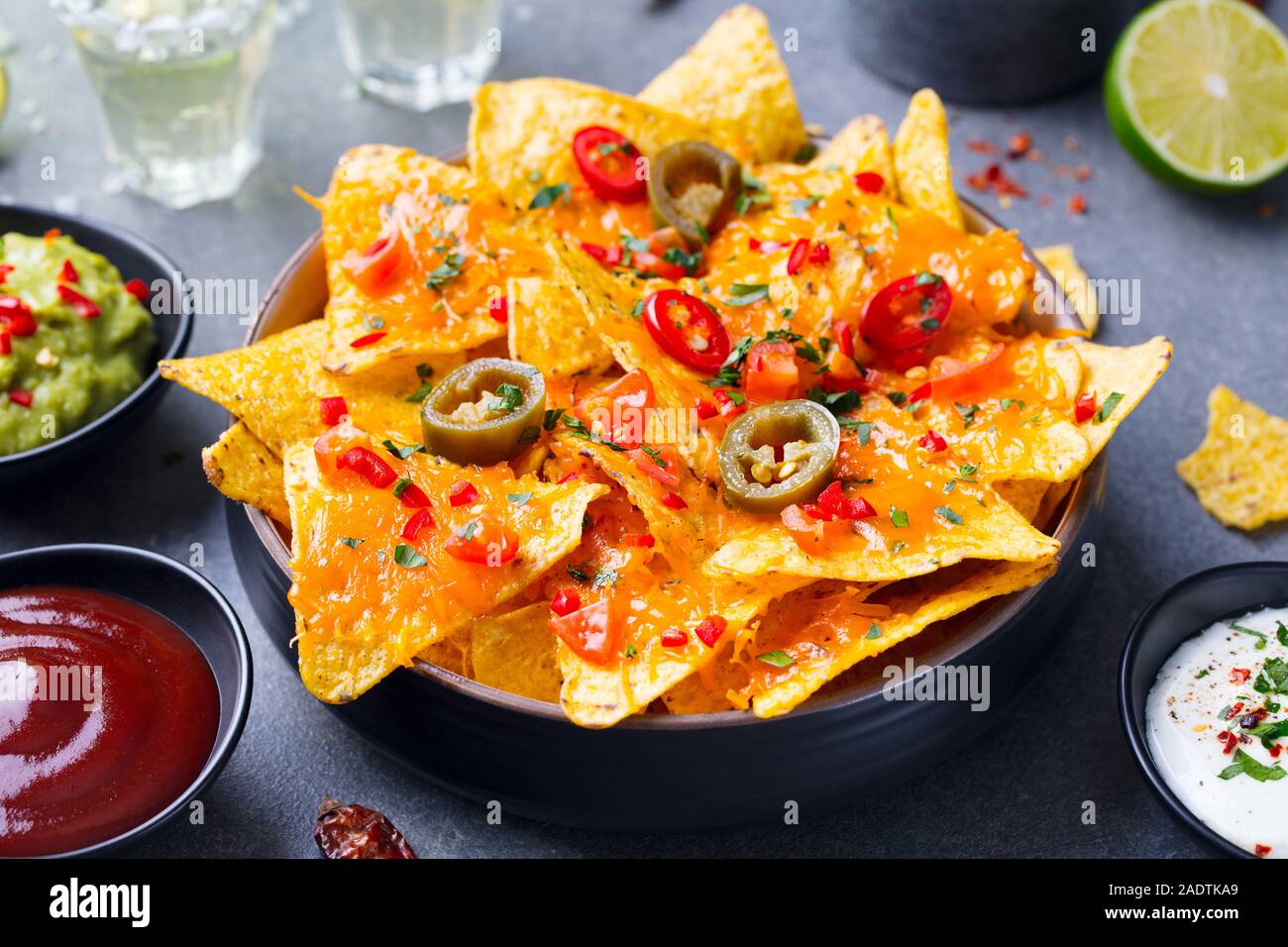 Nachos chips with melted cheese and dips variety in black bowl. Grey ...