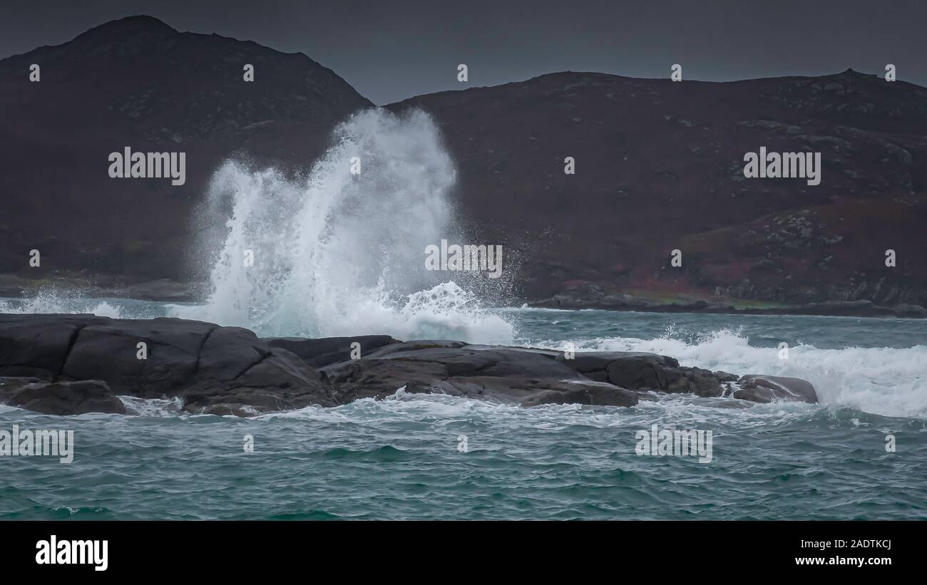 Huge wave splashing on rock on Sanna beach and mountains in background ...