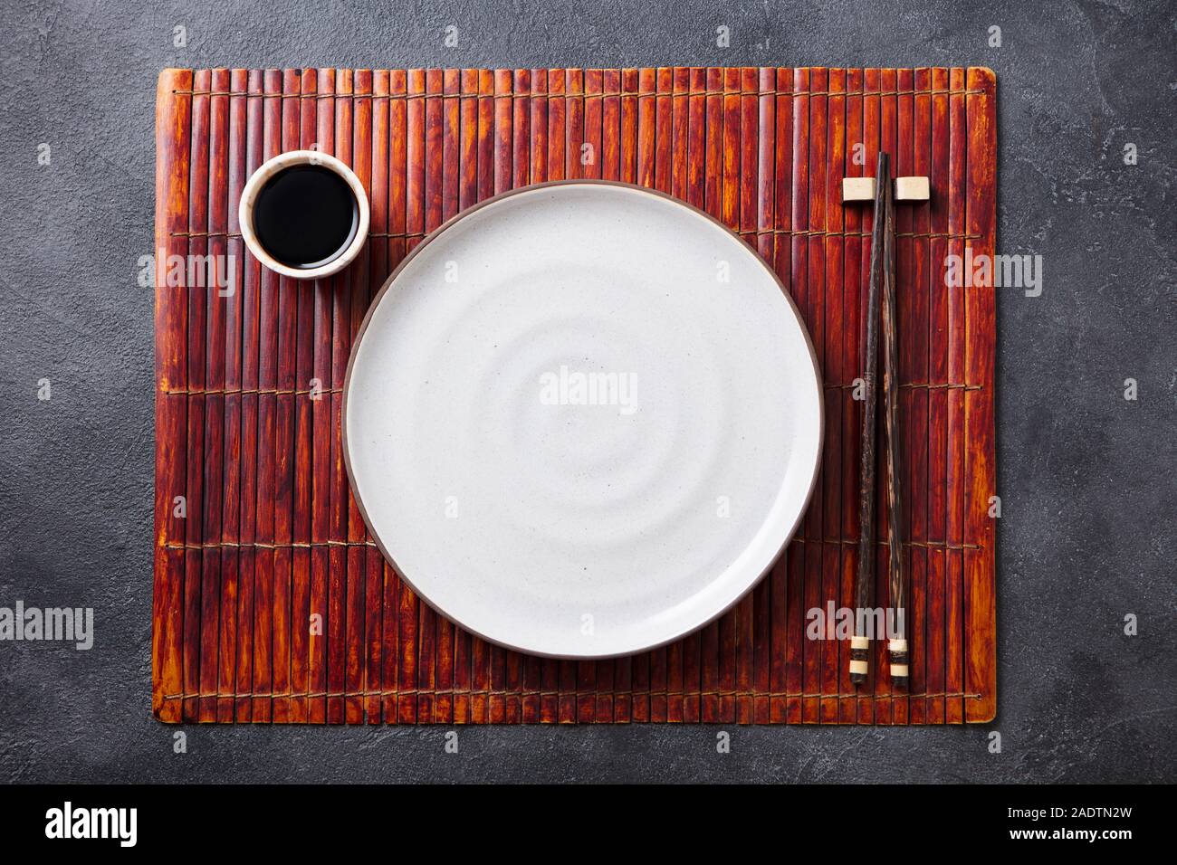 Asian table place setting with white plate, sauce bowl and chopsticks ...