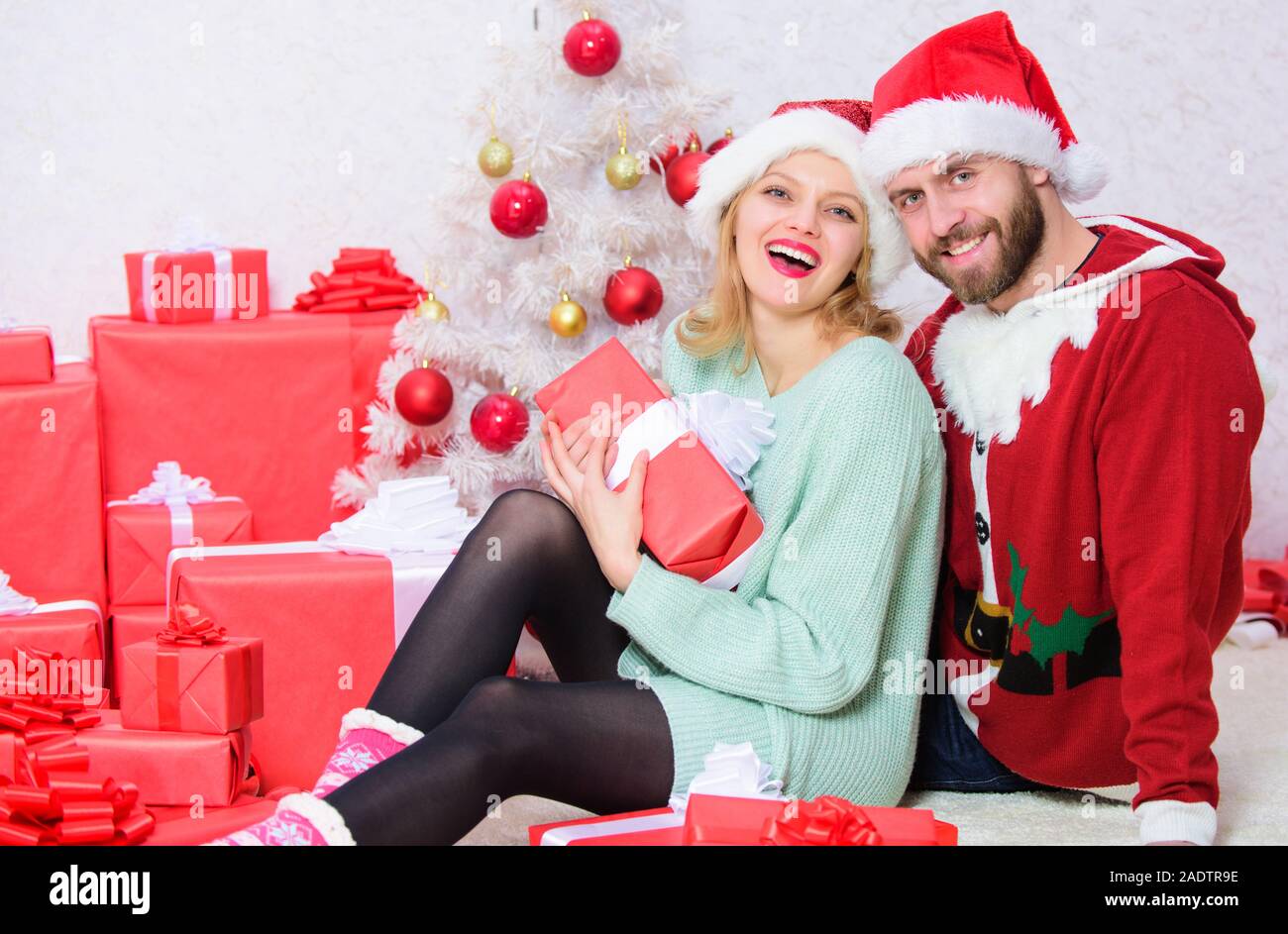 Loving couple cuddle smiling while unpacking gifts with christmas tree ...