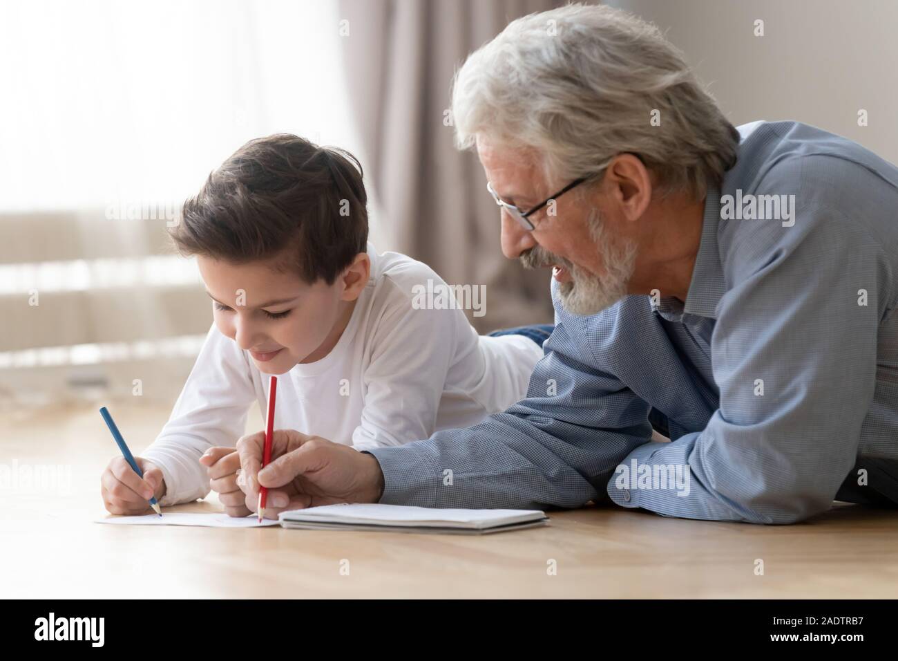 Grandfather drawing with grandson using colored pencils lying on floor ...