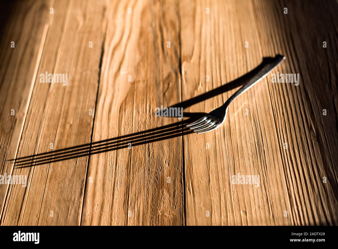 Dinner Fork throws large elongated Shadow on wooden table background ...