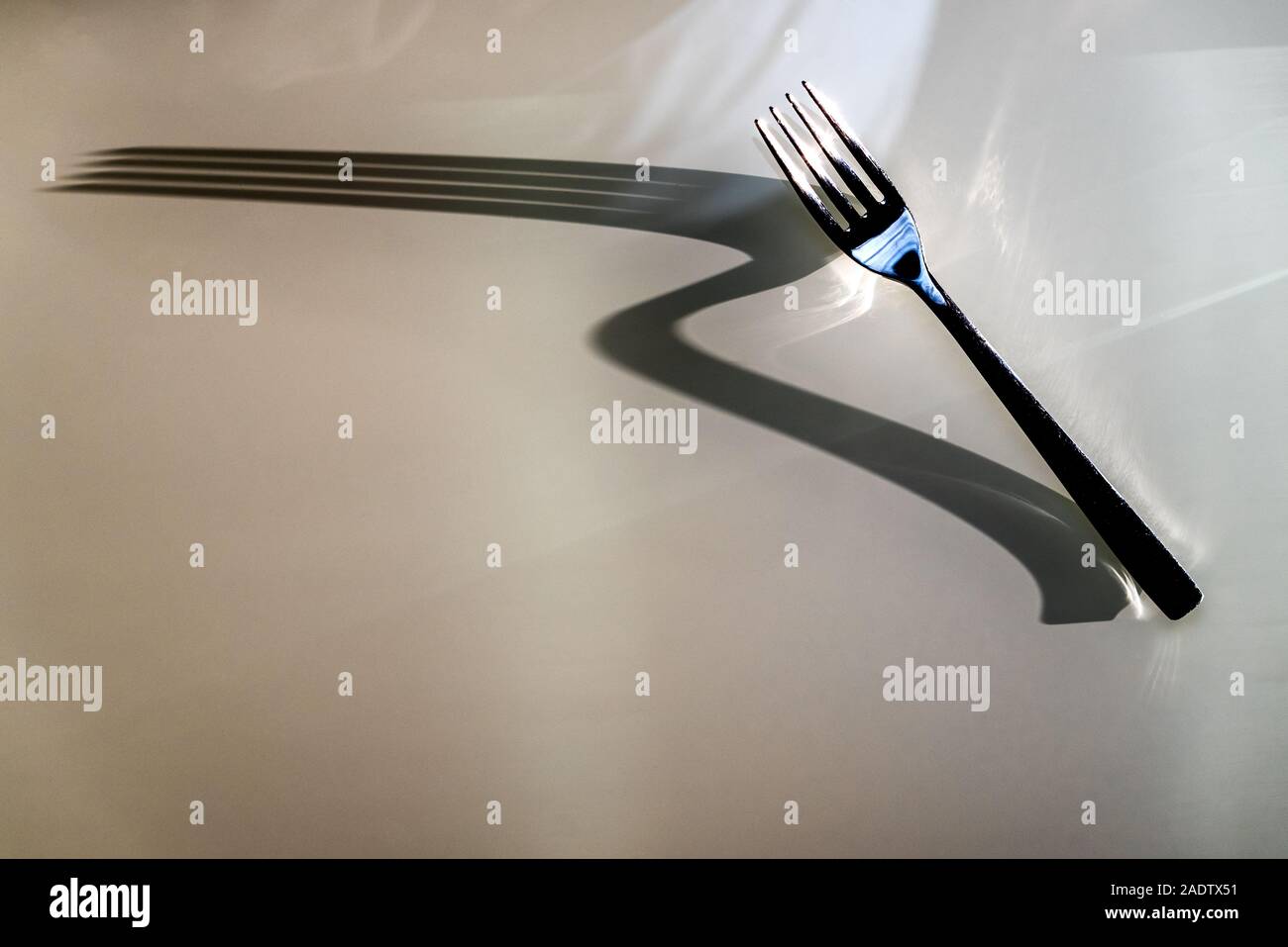 Fork throws large elongate Shadow on glass table background. Concept of ...