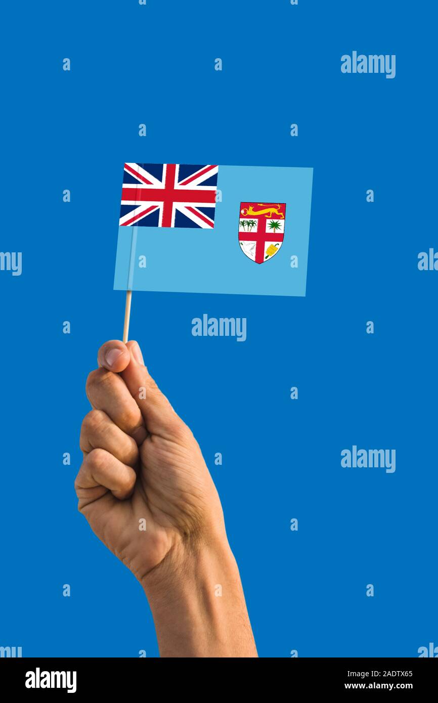 Woman hand holding Fiji flag with stick, waving flag on deep blue sky ...
